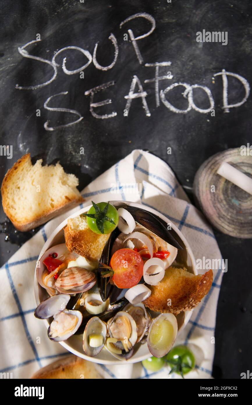 Presentation of a soup with seafood on a black background with writing ...