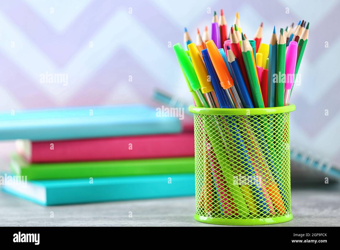 Books pens and markers in metal holder on colour background Stock Photo ...
