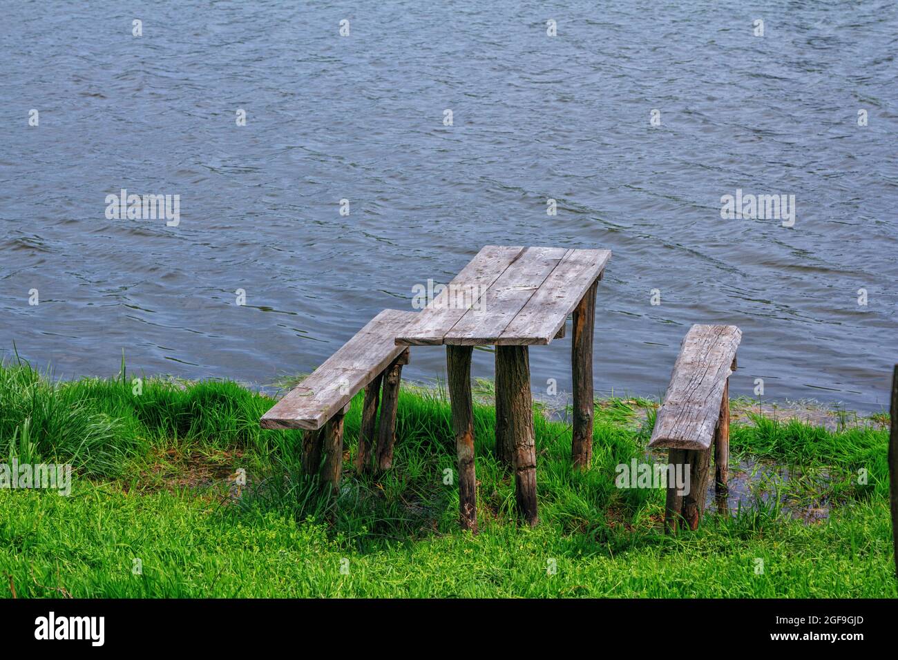 Wooden table and benches on a lake coast. Green grass and calm water ...