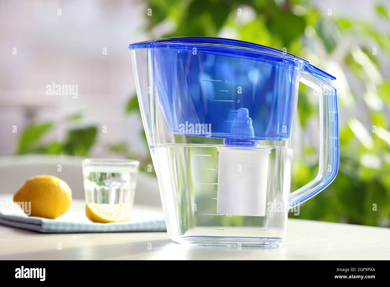 Water filter jug with lemon and glass on light wooden table Stock Photo ...