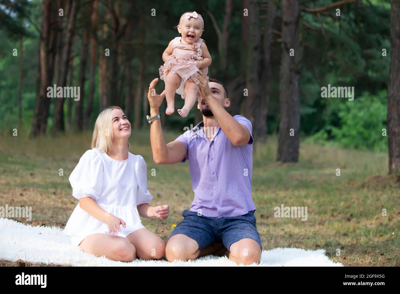 Husband, wife and their little daughter for a walk in the park. Happy dad and mom toss up their ...
