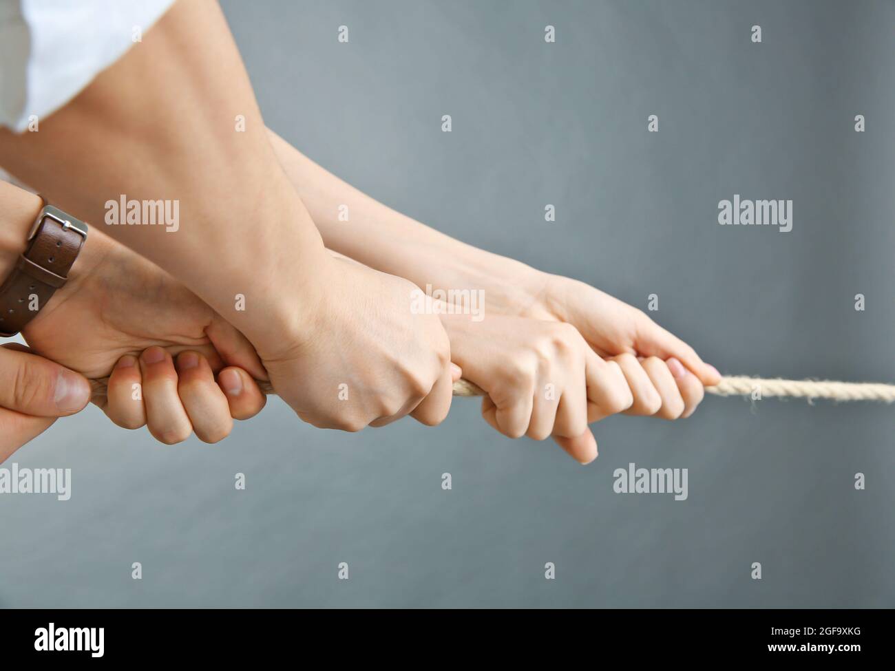 People hands pulling rope for playing tug of war on grey background ...