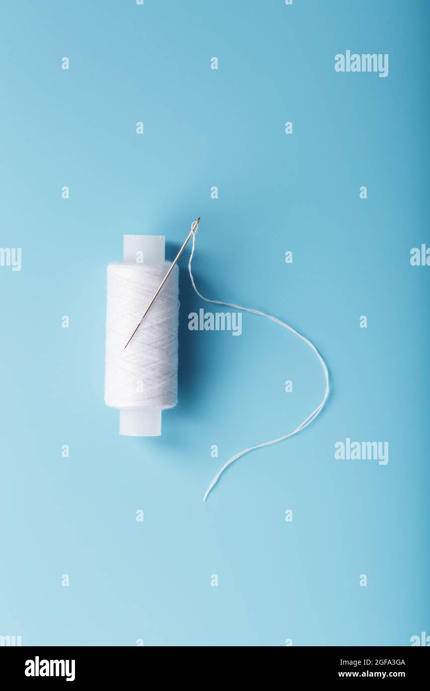 A spool of white thread with a needle on a blue background. Free space ...