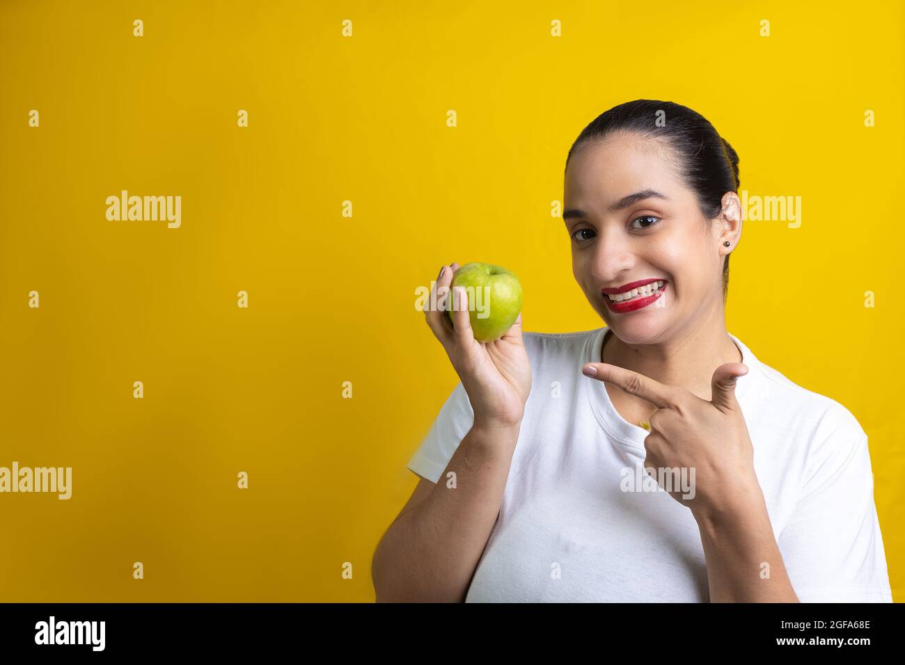 Funny Hispanic woman pointing to a green apple isolated on a yellow ...