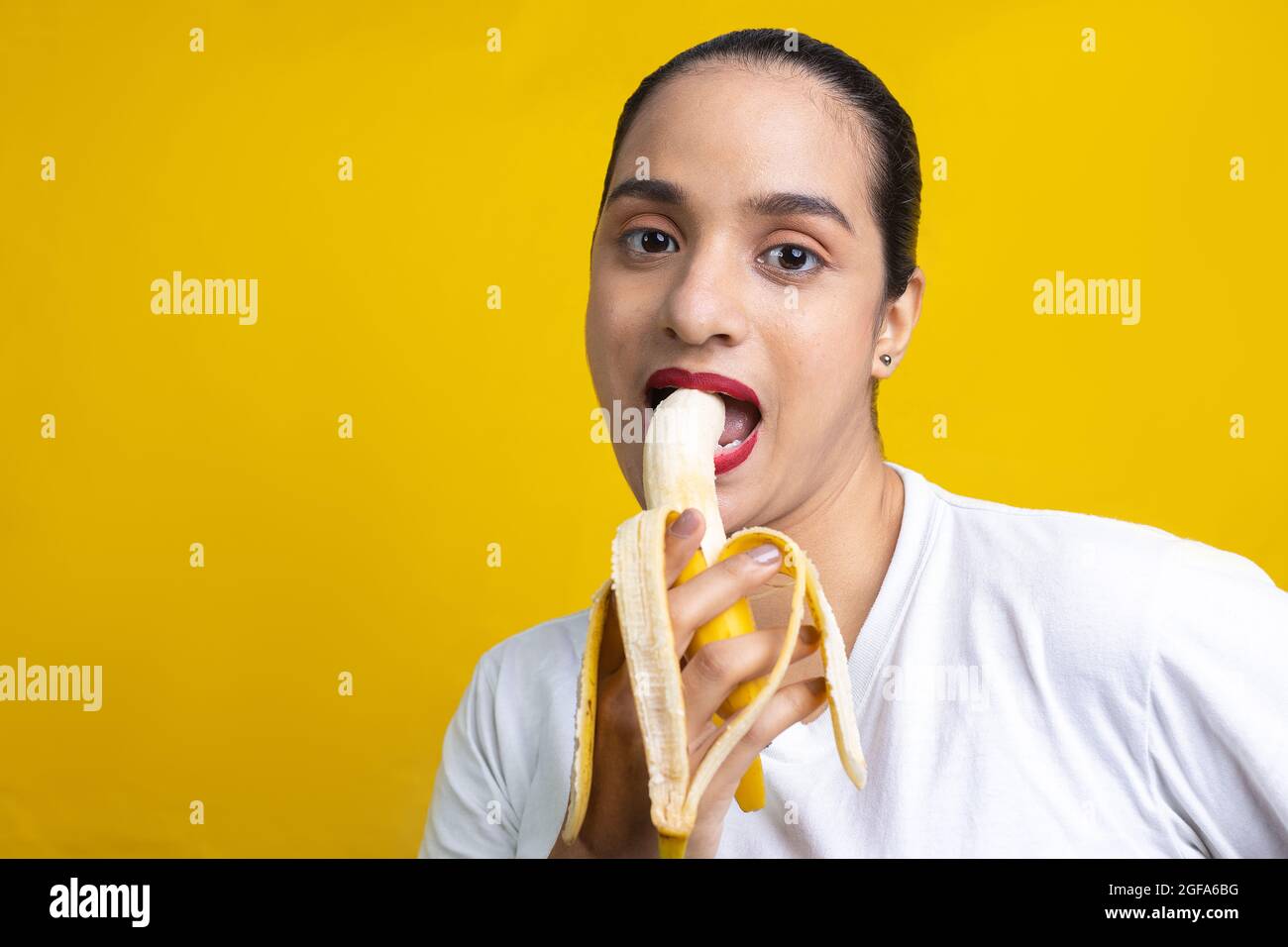 Funny Hispanic woman biting a banana isolated on a yellow background ...