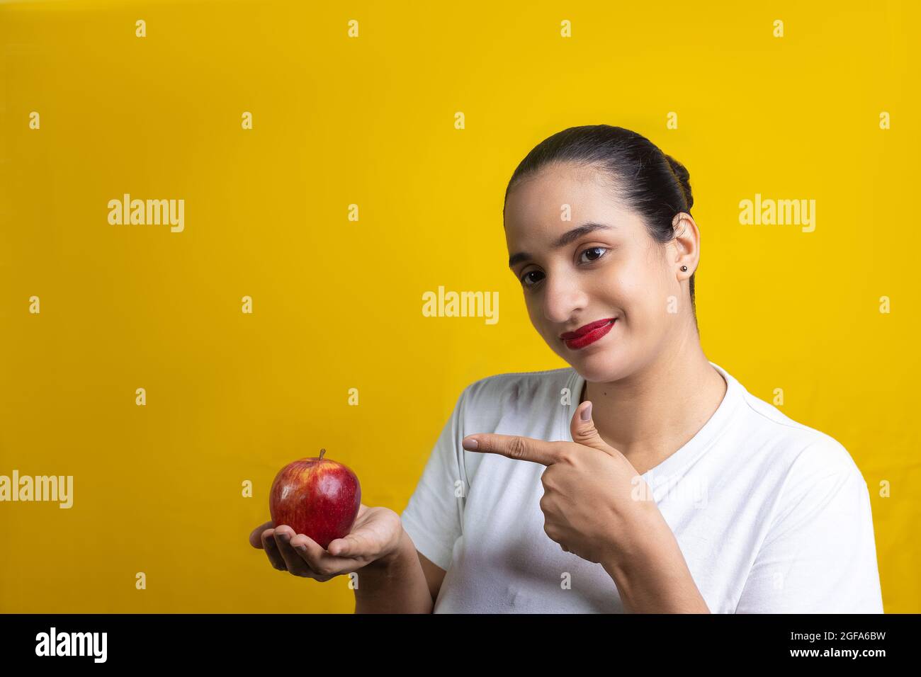 Funny Hispanic woman pointing to a red apple isolated on a yellow ...