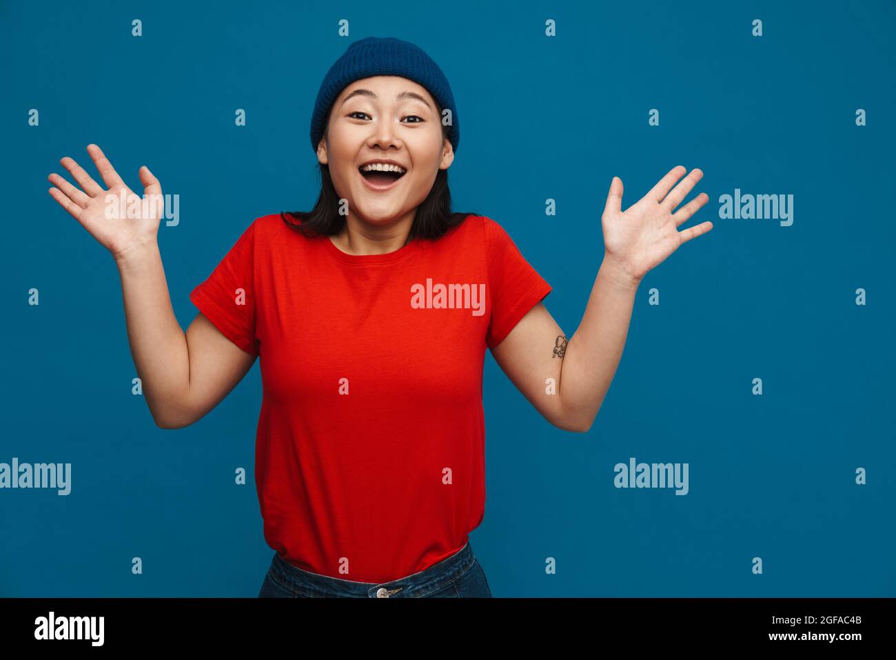 Excited asian teen girl in hat gesturing and smiling at camera isolated ...