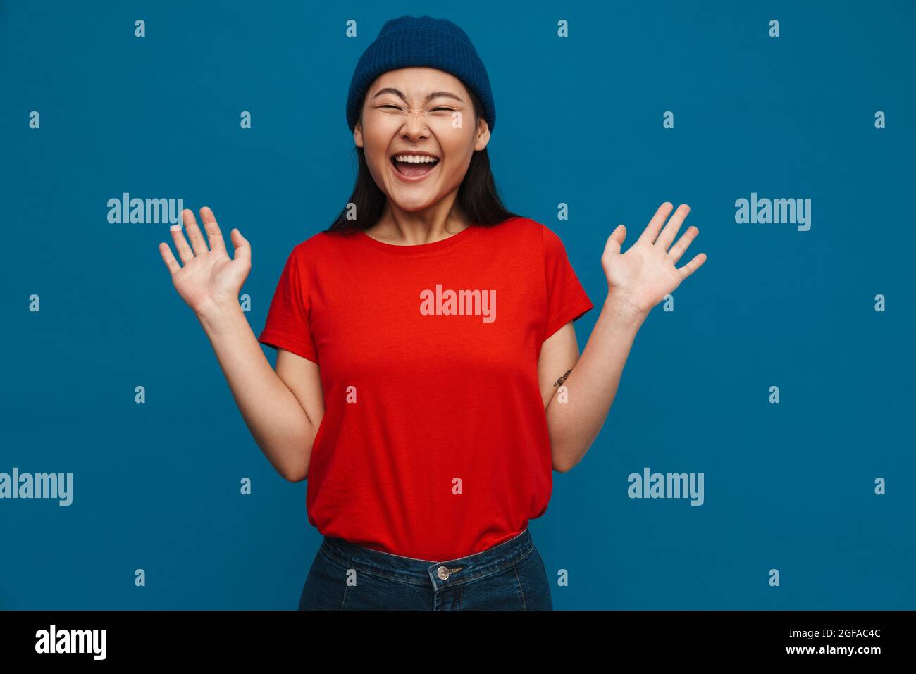 Excited asian teen girl in hat gesturing and laughing at camera ...