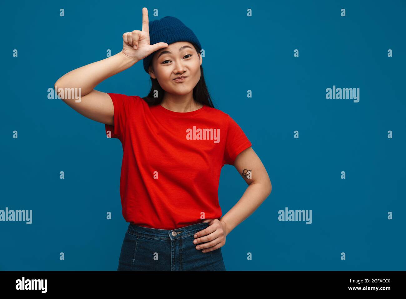 Asian teen girl in hat grimacing and pointing finger upward isolated ...