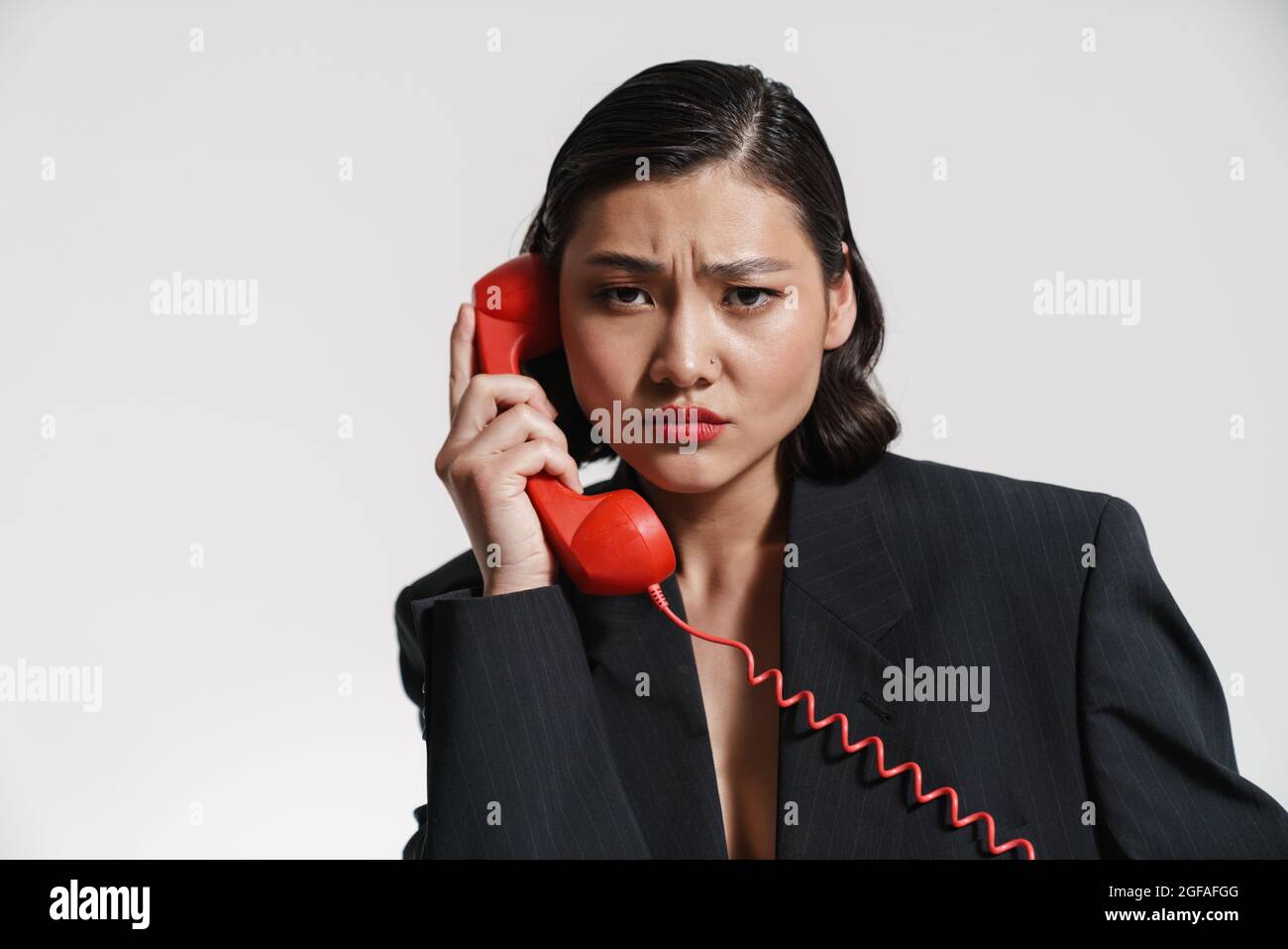 Brunette asian woman wearing jacket frowning while talking on retro ...