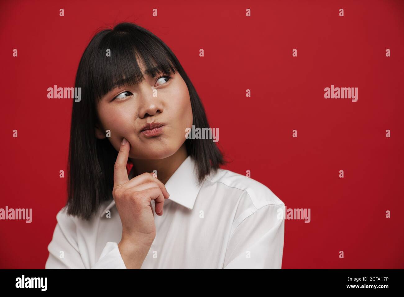 Young asian woman pointing finger at her cheek and looking aside ...