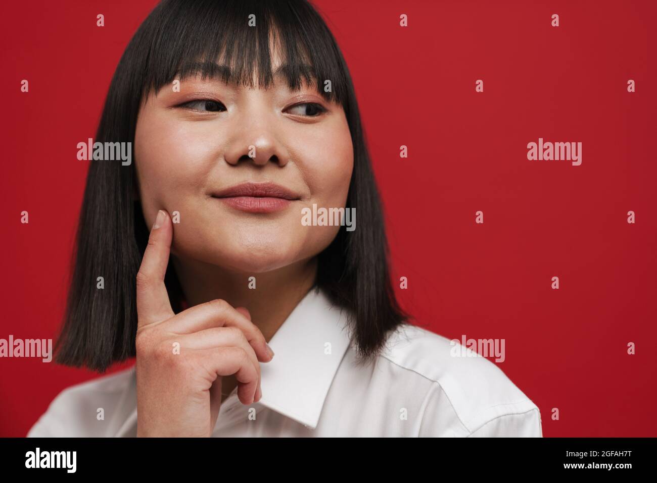 Young asian woman pointing finger at her cheek and looking aside ...