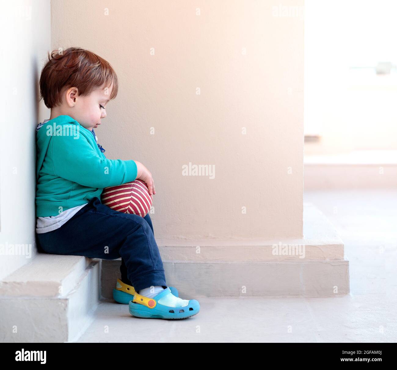 Pensive small boy sitting with a ball on his lap. Little boy leaning on ...