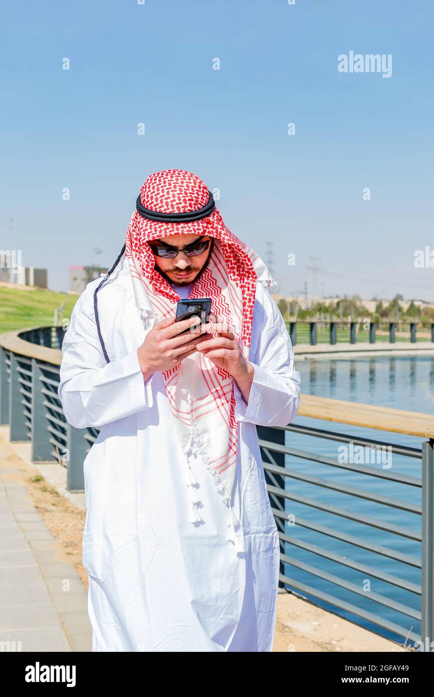 Arab man in traditional garb and red keffiyeh using his smartphone on a ...
