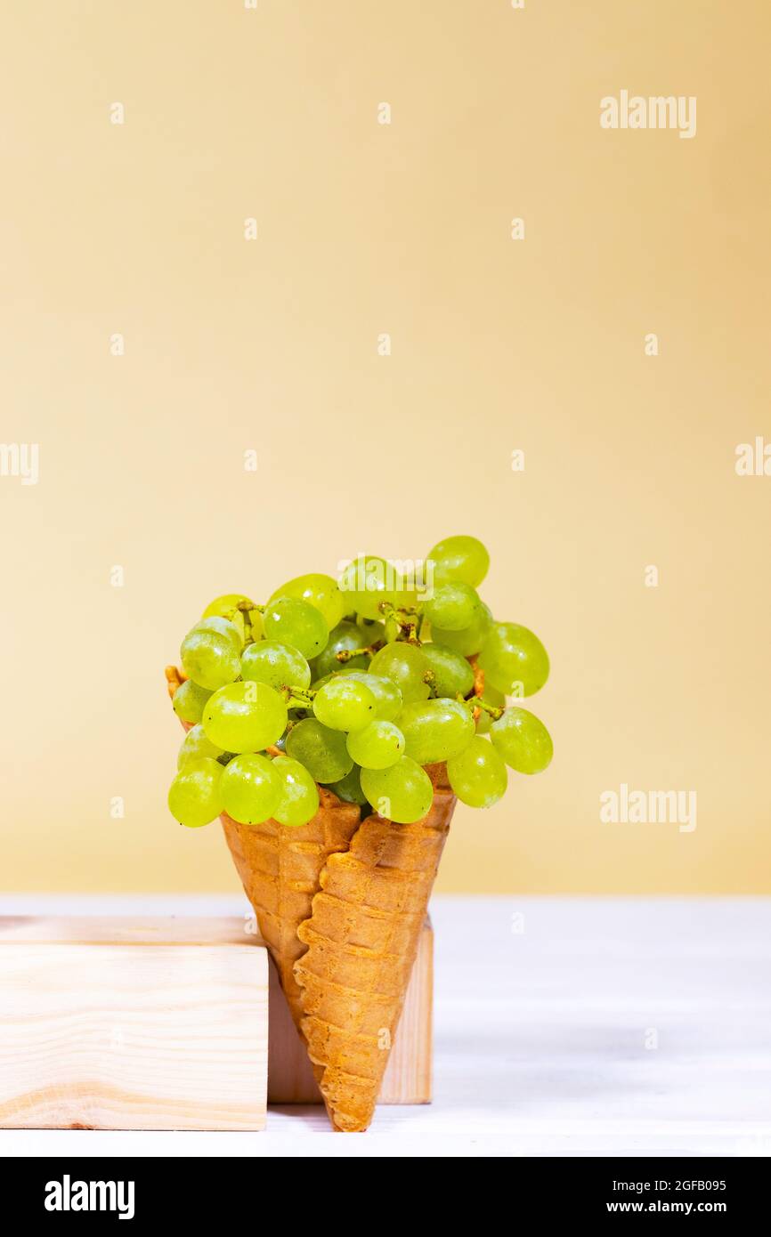 Green grape in sweet wafer cone on wooden stands over light orange ...