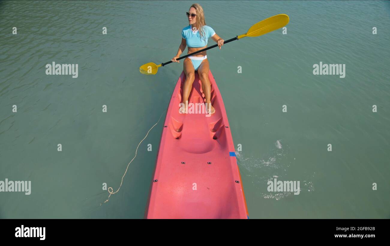 Pretty sportive blonde lady in stylish swimsuit sails on pink plastic ...