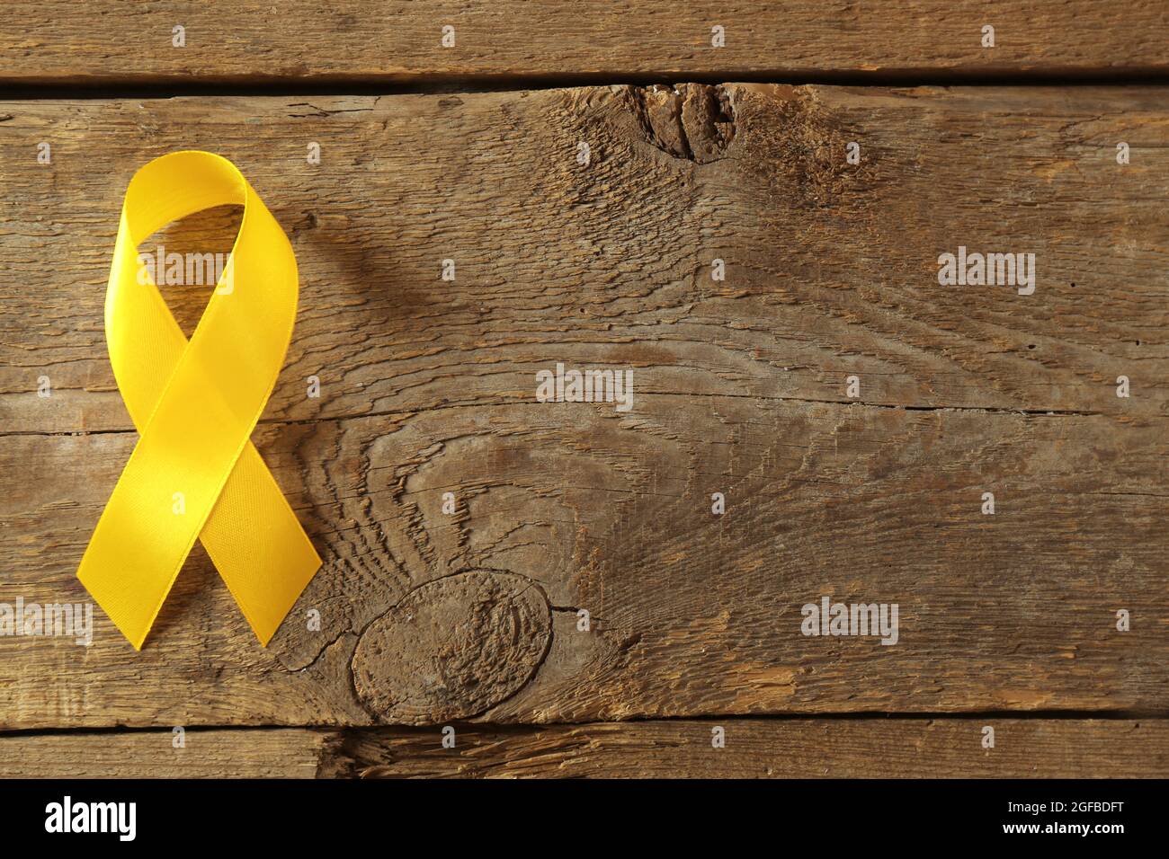 Yellow awareness ribbon on wooden background Stock Photo - Alamy