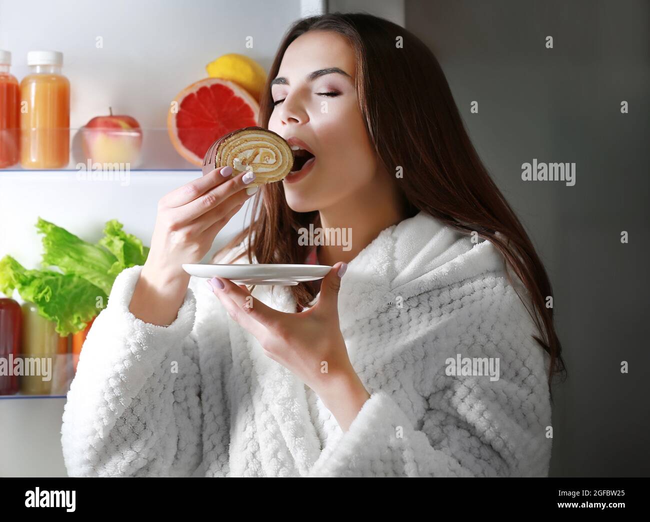 Young beautiful woman eating unhealthy food from the fridge at night ...