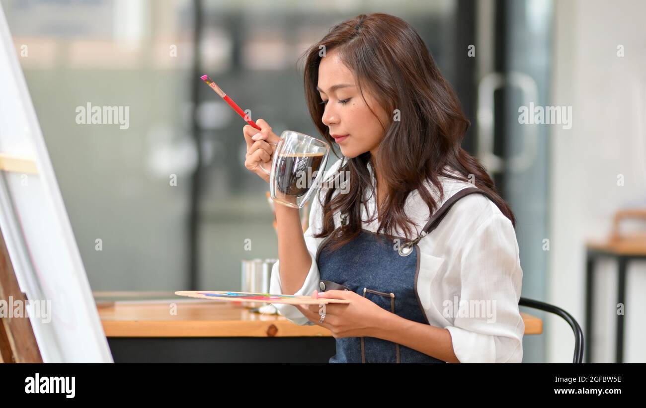 Attractive female artist drink coffee, taking break from art piece ...