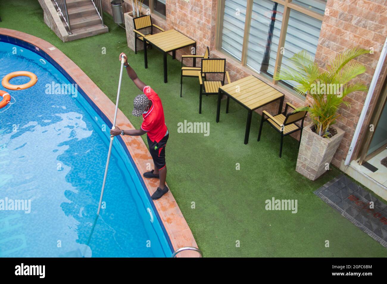 Cleaning of swimming pool by pool-guy, using net. Decorative plants ...