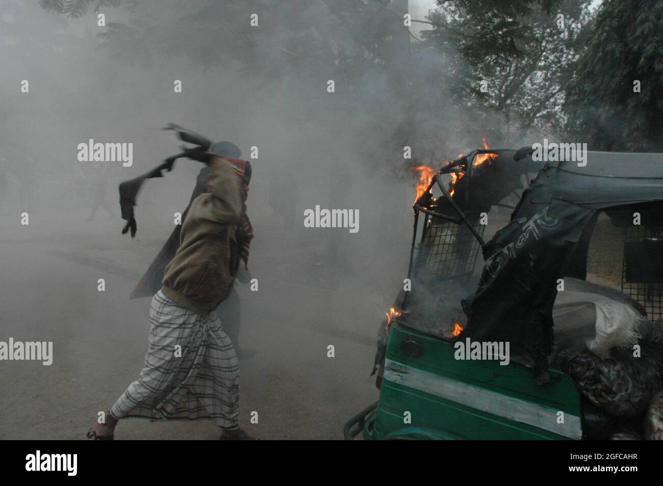 A man chasing after a burning three-wheeler at a riot. Bangladesh Stock ...