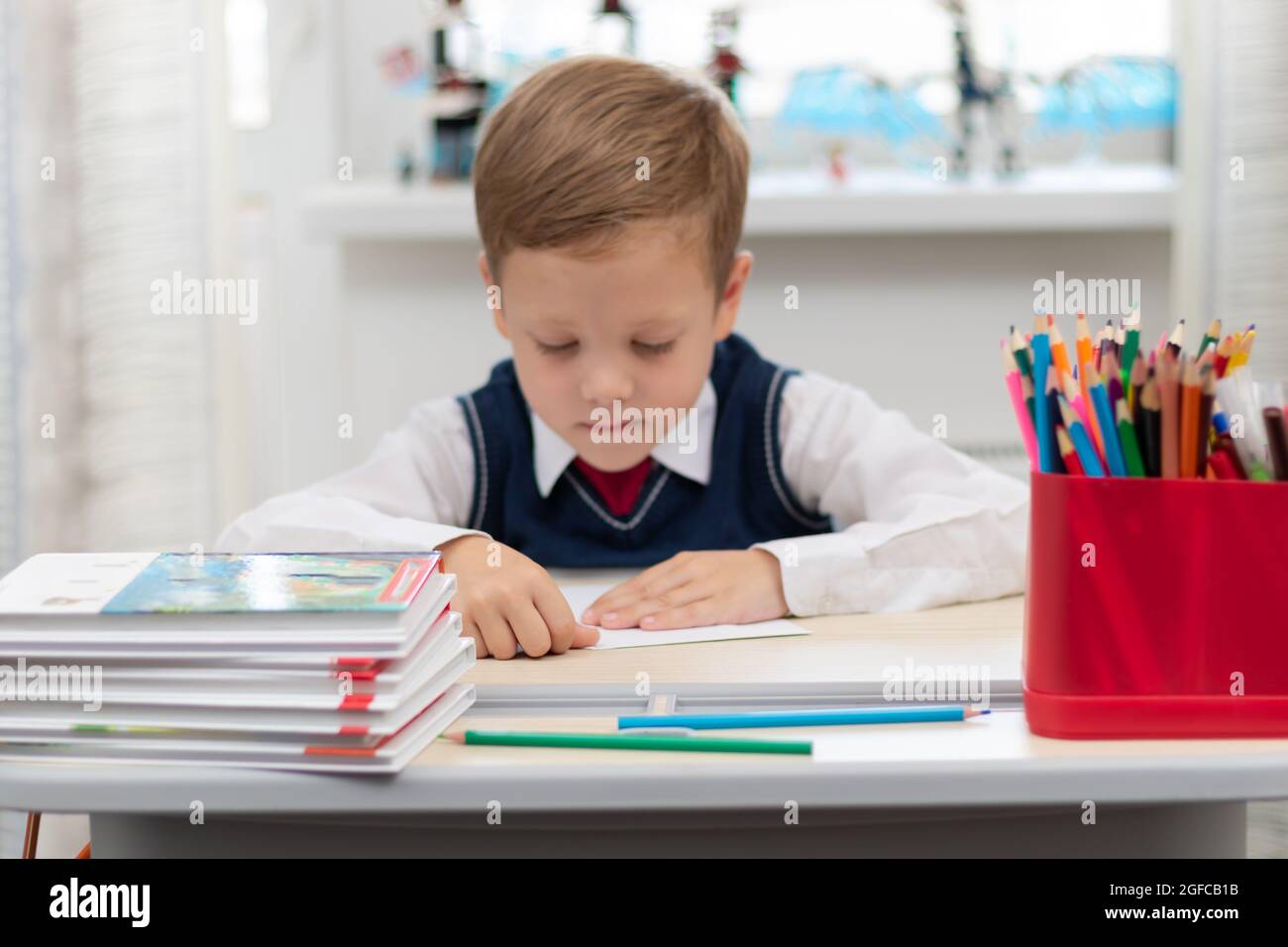 A cute first-grader boy in a school uniform at home while isolated at ...