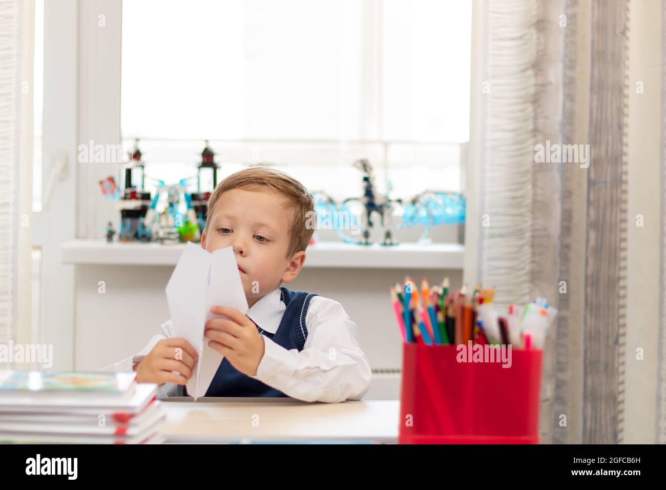 A cute first-grader boy in a school uniform at home while isolated at ...