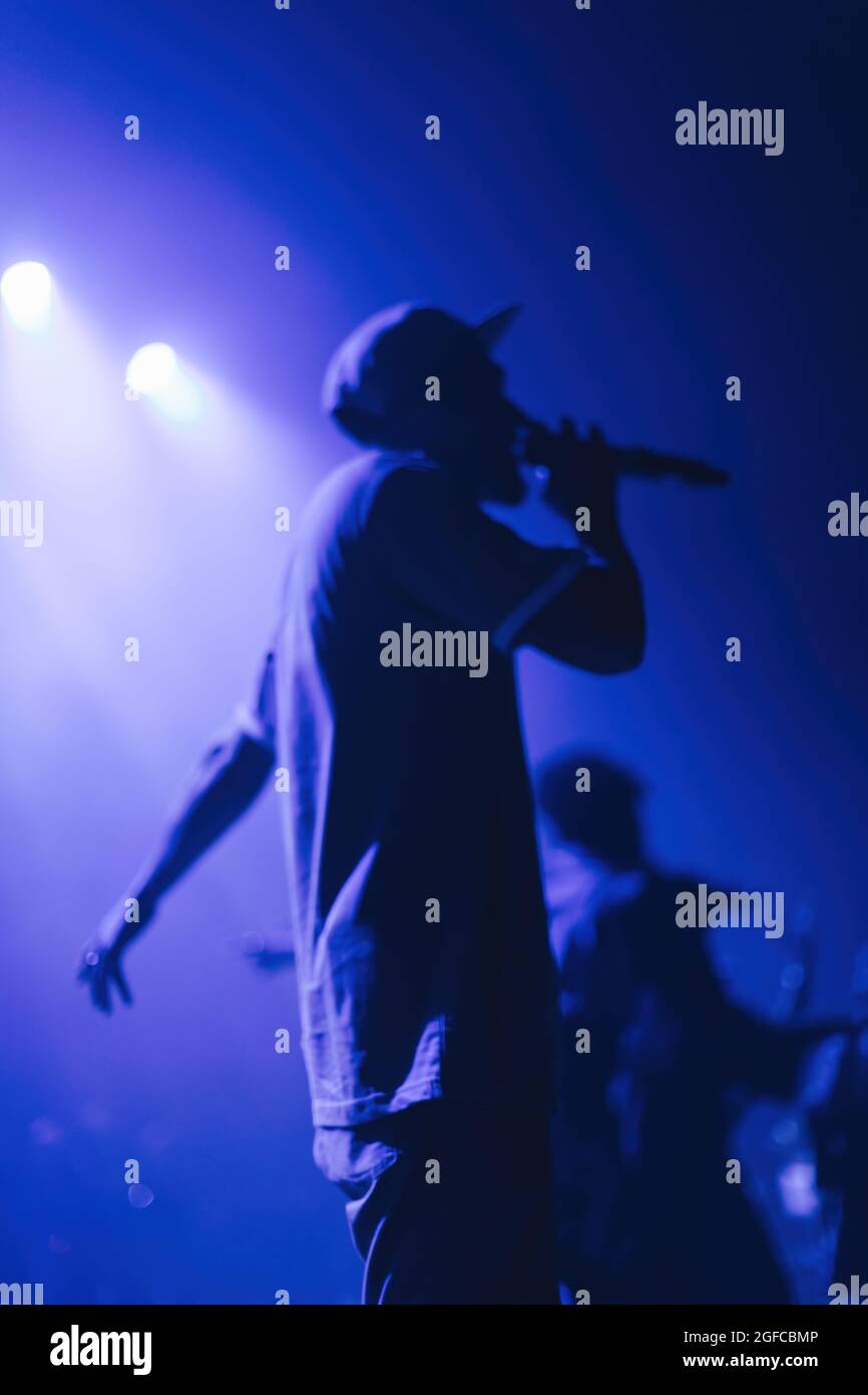 Blurred singer with microphone on stage with blue rays of light ...