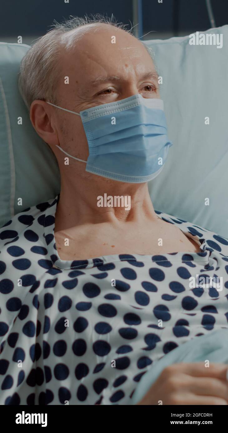 Portrait of unwell patient in hospital ward bed sitting with oximeter ...