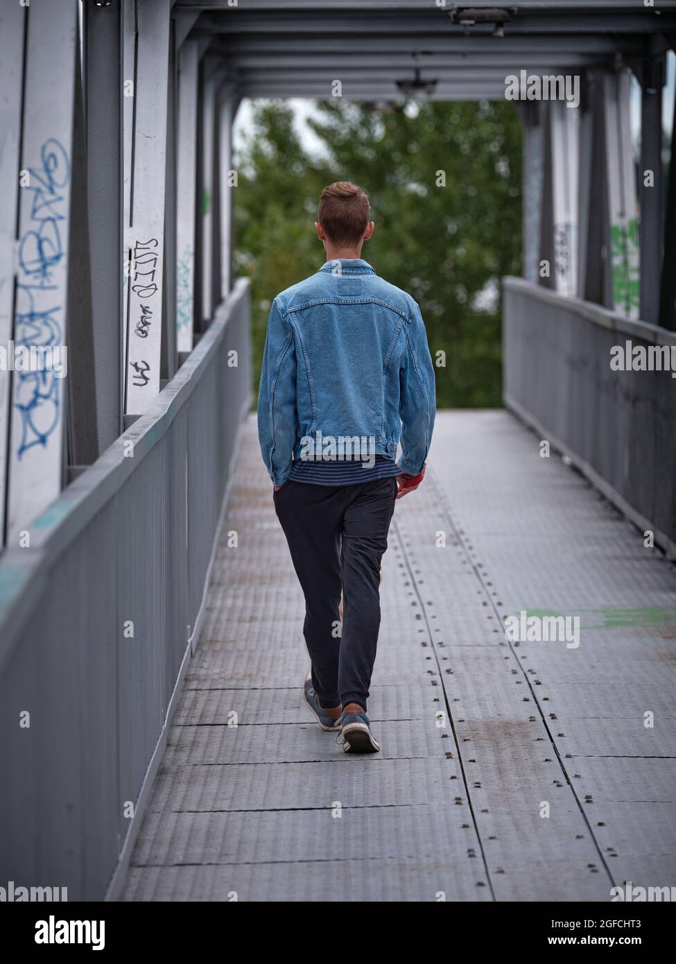 A young man from behind walks over a metal bridge Stock Photo - Alamy
