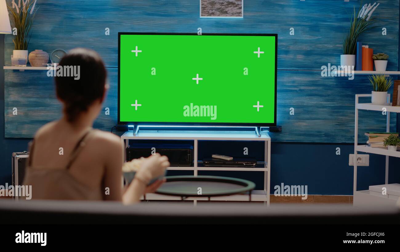Woman looking at tv designed with green screen mockup template and ...
