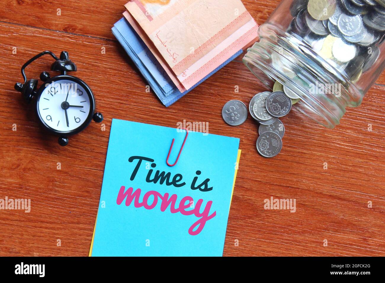 Close up of alarm clock, coins, banknotes and paper with text TIME IS ...