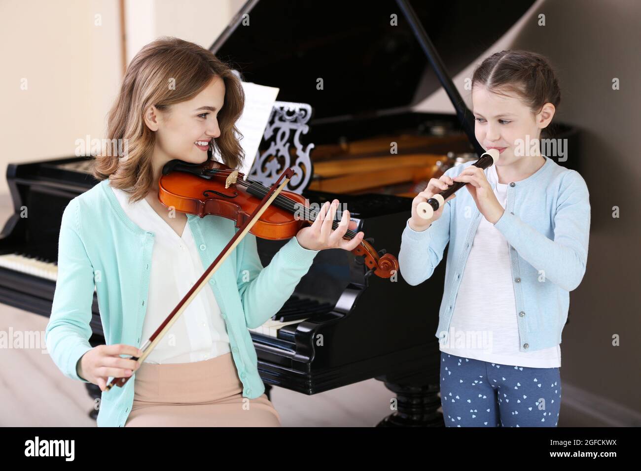 Two girls playing violin and flute on piano background Stock Photo - Alamy