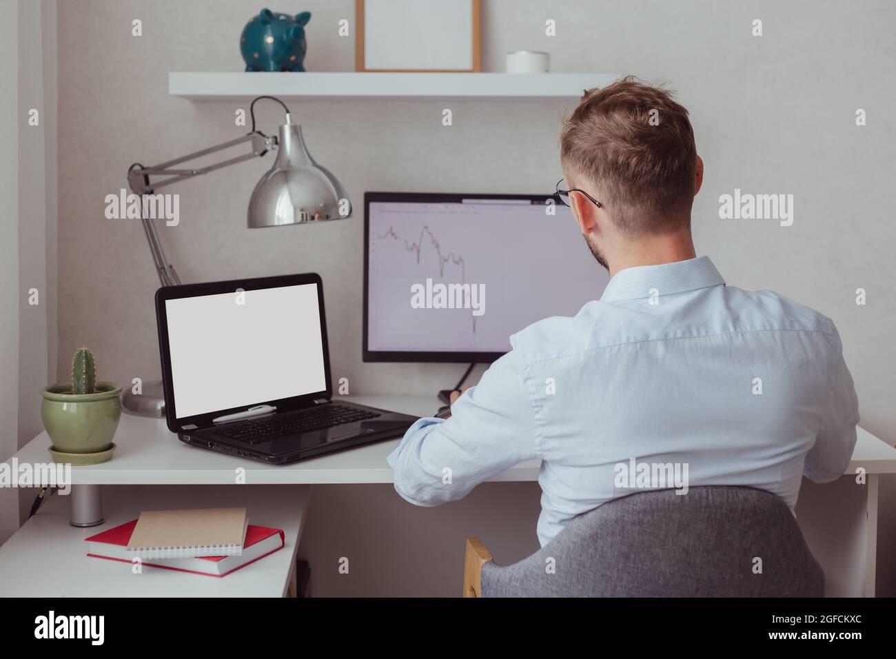 Man working, looking at technical charts on pc and laptop with blank ...