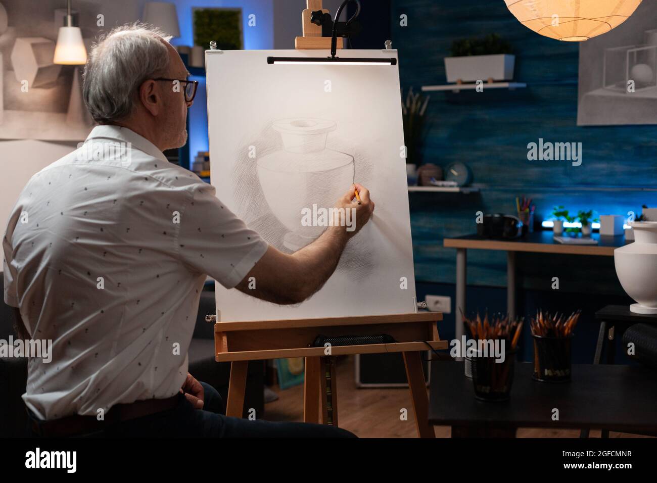Elderly artist working on vase drawing with pencil on canvas and easel ...