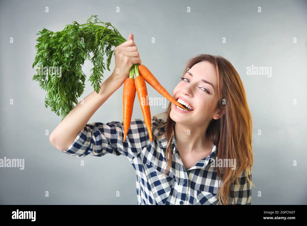 Beautiful girl eating carrot on grey background Stock Photo - Alamy