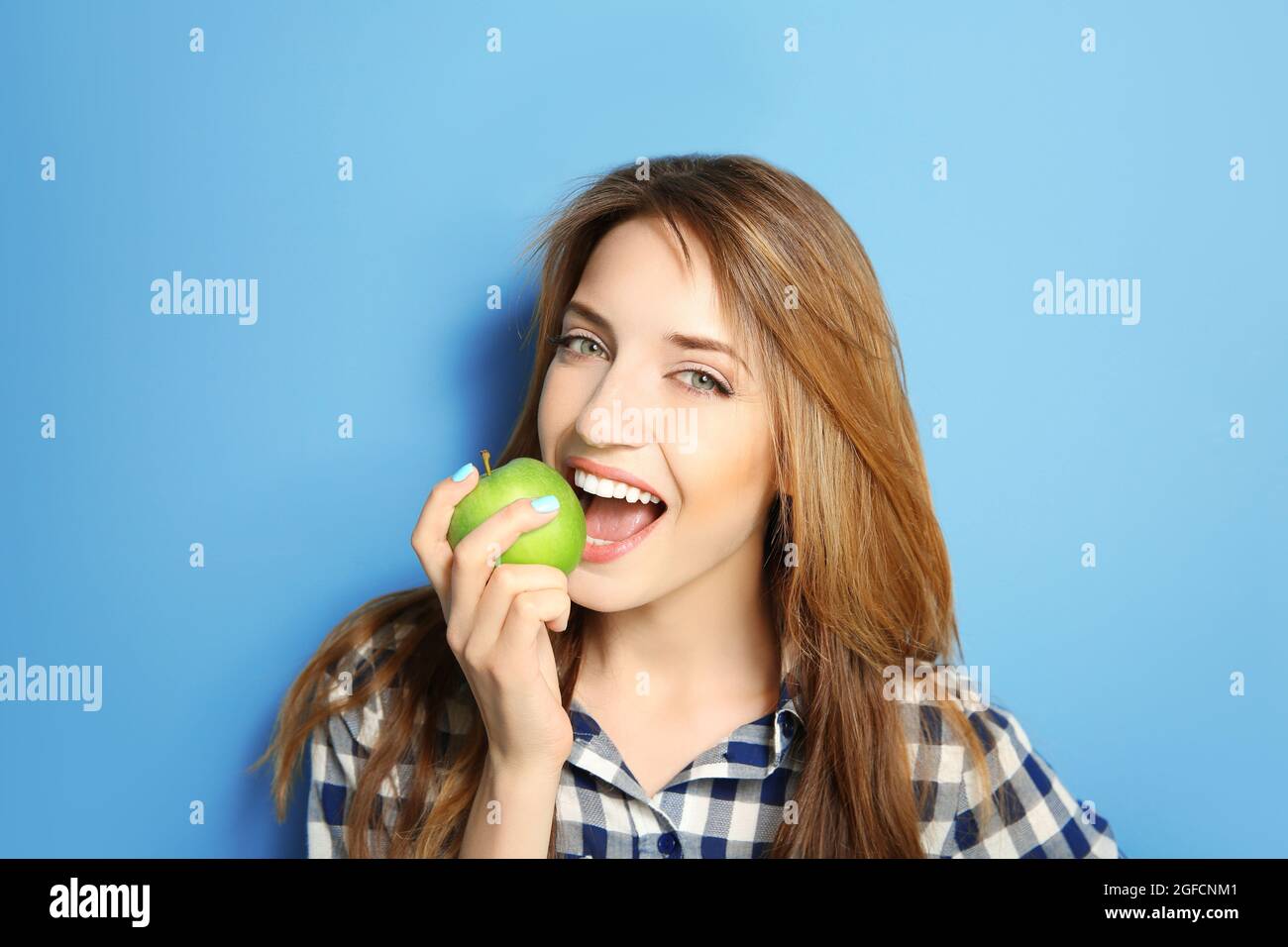 Beautiful girl eating apple on blue background Stock Photo - Alamy