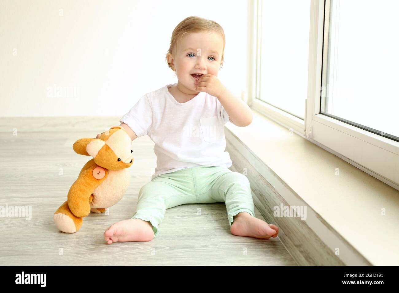 Baby sitting with teddy bear at window in room Stock Photo - Alamy