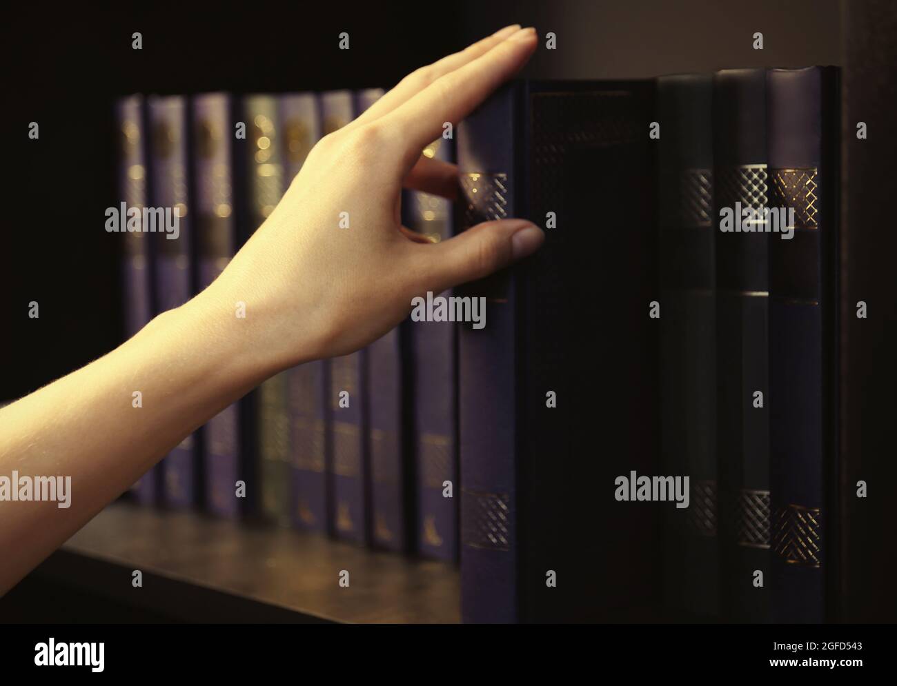 Books in a row on a bookshelf. Hand taking a book Stock Photo - Alamy