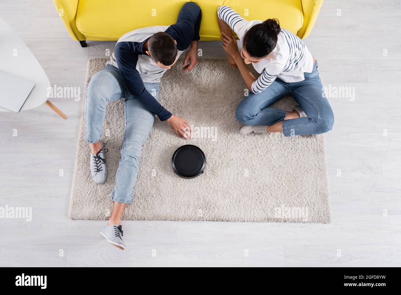Overhead view of multiethnic couple sitting near robotic vacuum cleaner ...
