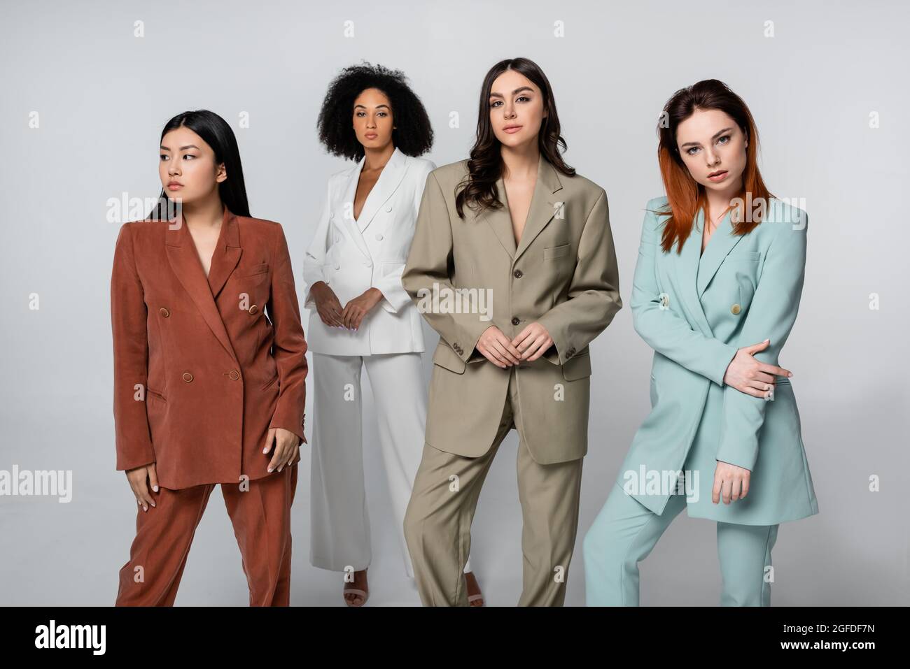 multiethnic group of young models in pastel color suits posing on grey ...