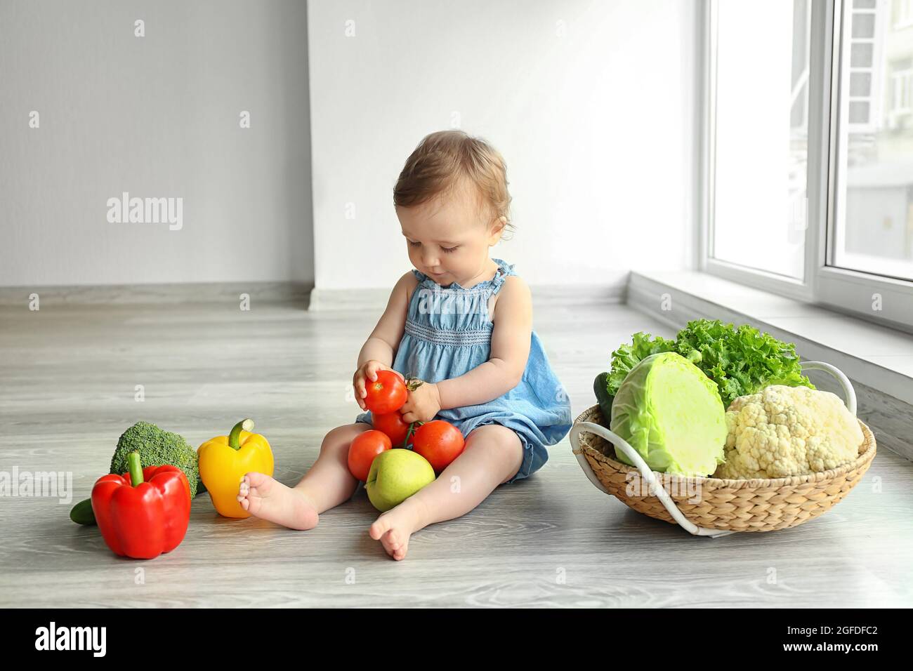 Cute baby girl with vegetables on wooden floor Stock Photo - Alamy