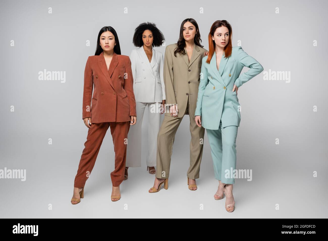 full length of multiethnic group of models in pastel color suits posing ...