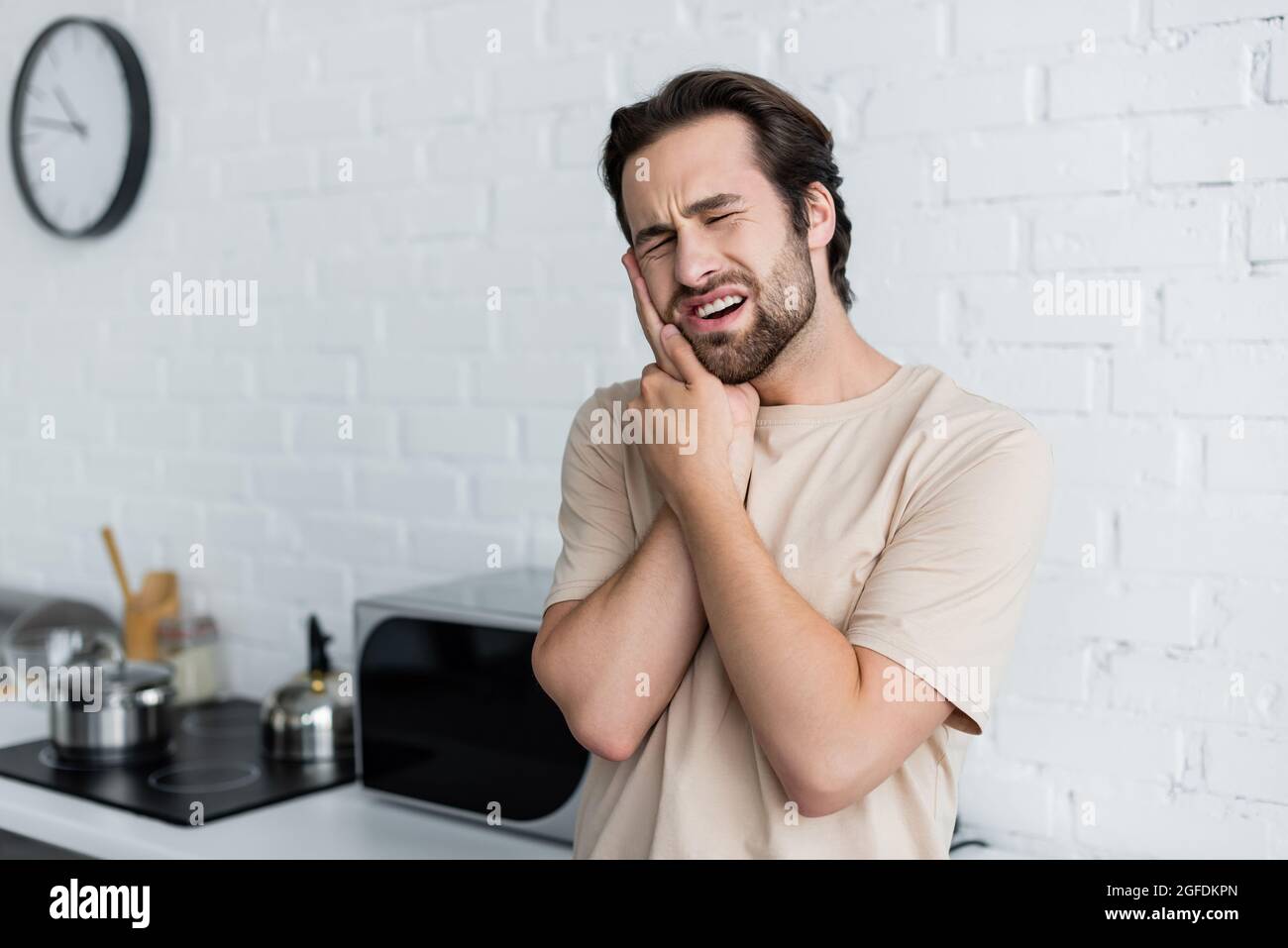 Man suffering from toothache while touching cheek Stock Photo - Alamy