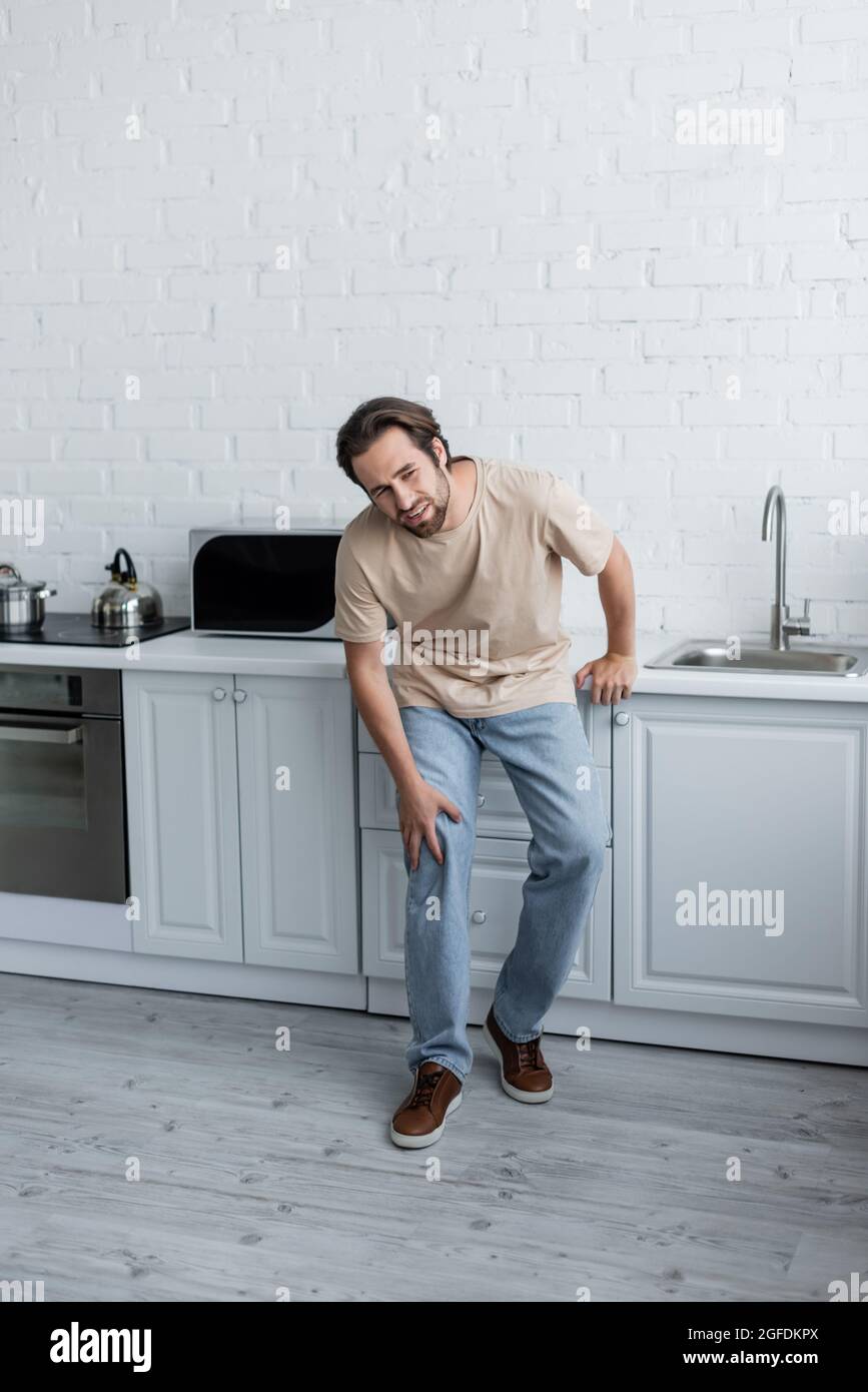 Diseased man touching knee on kitchen Stock Photo - Alamy