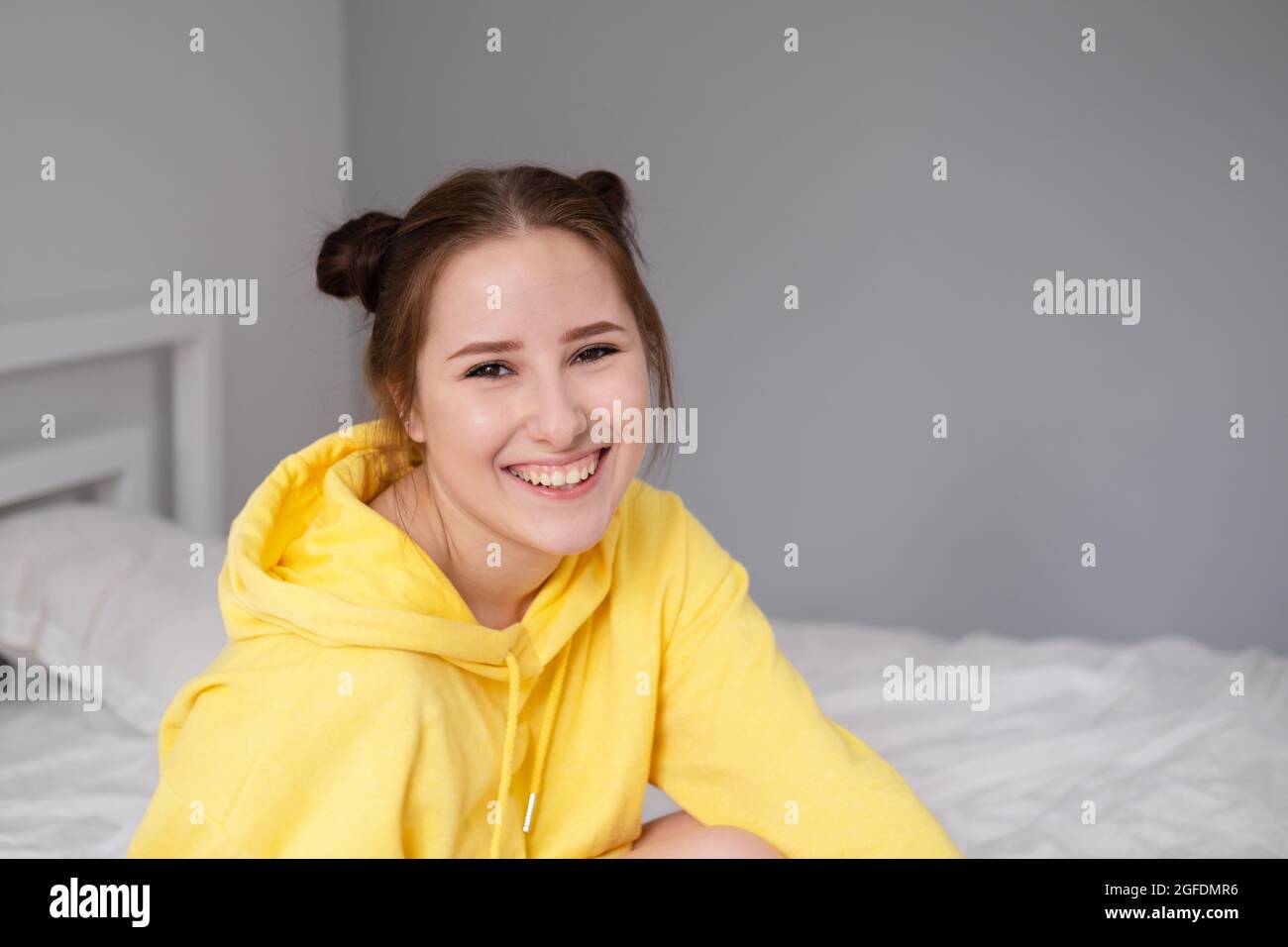 happy cheerful brunette girl in yellow hoodie in white bedroom sitting ...