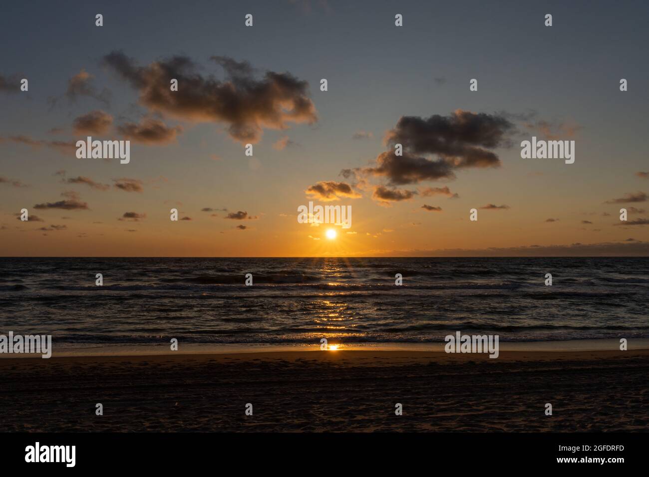 colorful beach sunset with the sun dropping into the ocean under an ...
