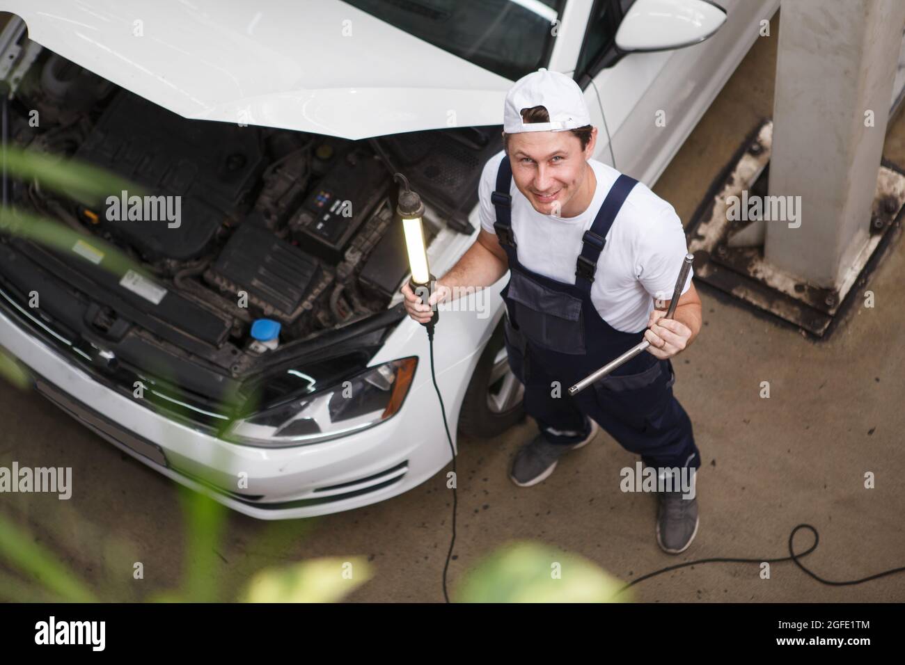 Professional car mechanic smiling to the camera while repairing an auto ...