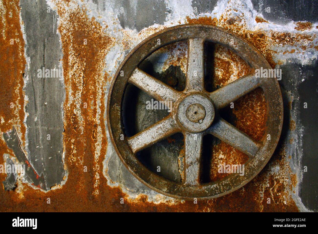 Rusty six-pronged wheel set into an old rusty metal wall background ...
