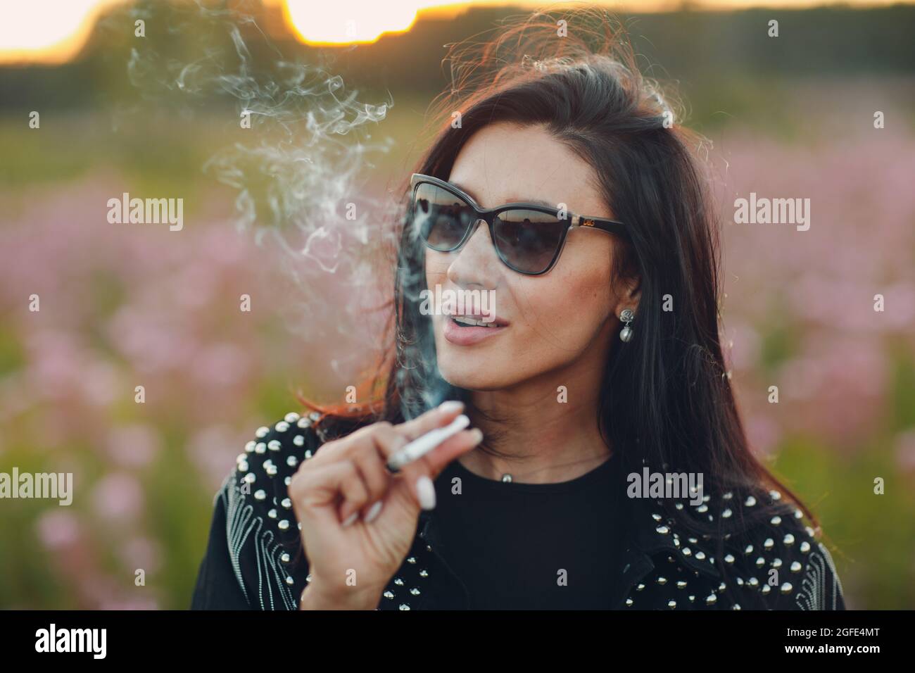 Young woman smoking on blooming Sally flower field. Lilac flowers and ...